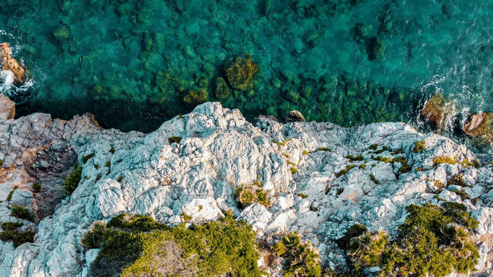 Aerial Turquoise Sea Over Rugged Coastal Cliffs and Sunlit Rocks - backiee