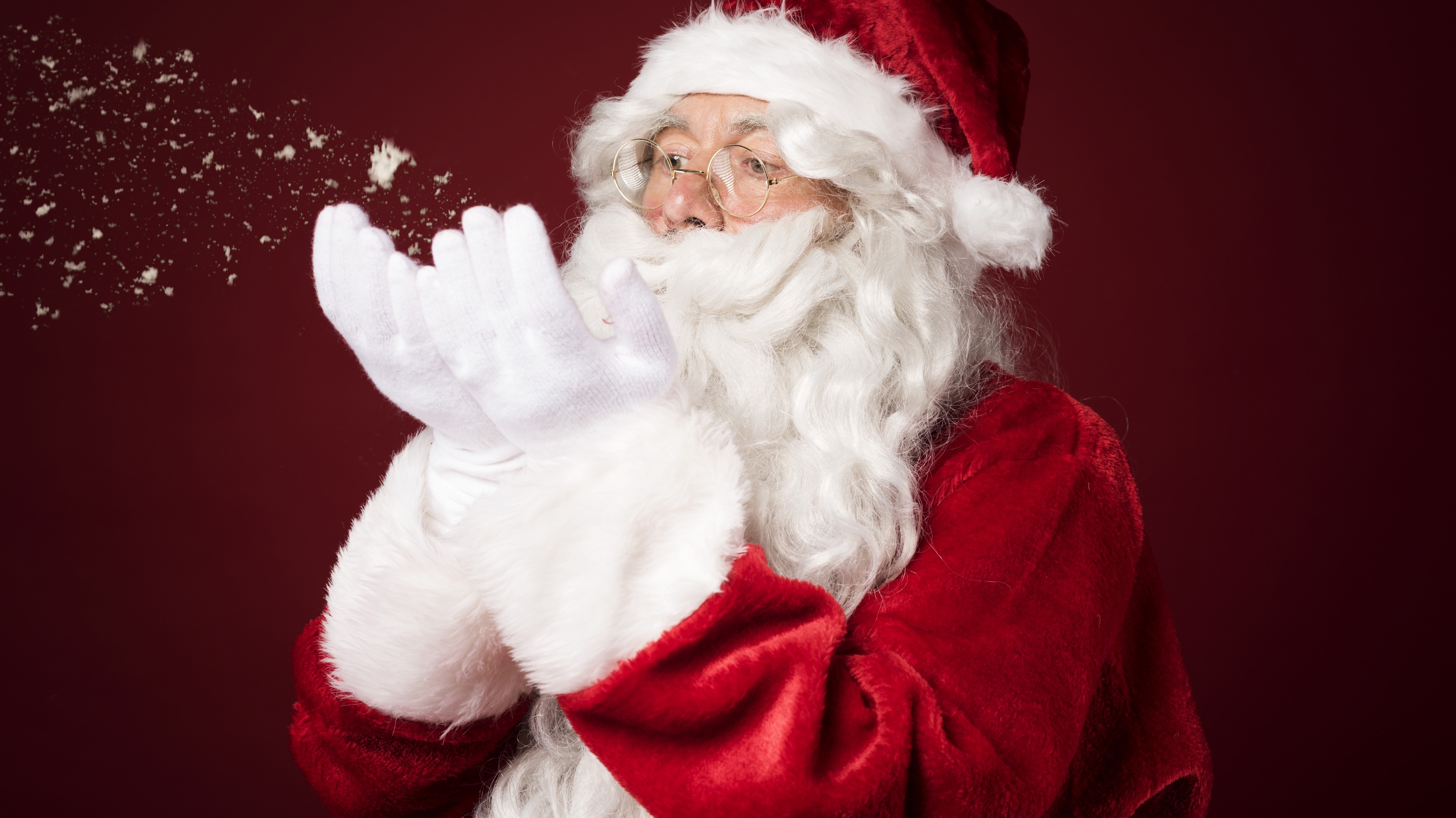 Santa Claus Blowing Snowflakes on Deep Red Christmas Background - backiee